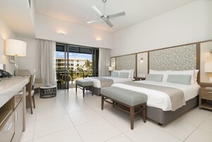 Quarto de hotel com cama grande, escrivaninha, cadeira e varanda com vista para prédios.