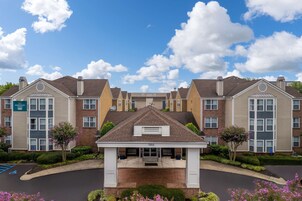 Entrada de hotel com acesso coberto, vários edifícios e céu claro.
