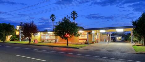 Um motel bem iluminado com área de estacionamento coberta, céu claro e placa de limite de velocidade visível.