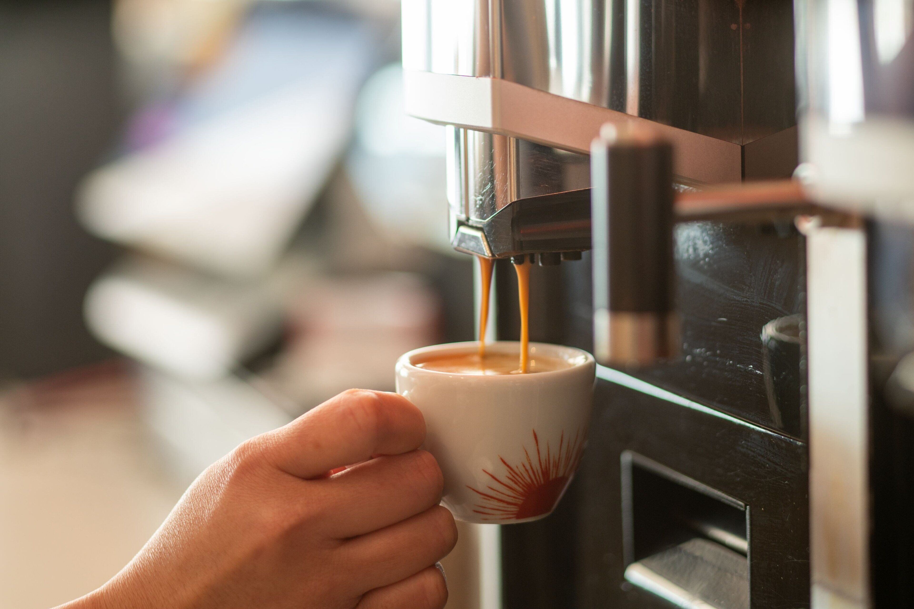 Mão segurando uma xícara sob uma máquina de café, com café sendo servido.