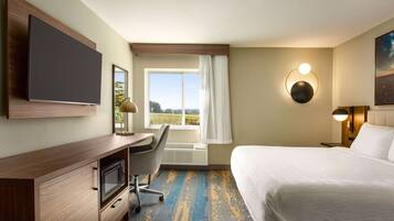 Quarto de hotel com cama, escrivaninha, cadeira, televisão de tela plana e uma janela grande com cortinas.