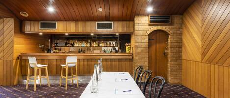 Uma sala de conferências com uma mesa comprida, cadeiras, um espaço de bar com garrafas e uma parede de tijolos.