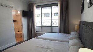 Quarto de hotel com duas camas, televisão, janela com cortinas e abajur.