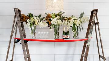 Uma mesa de escada de madeira rústica com um prateleira vermelha, decorada com flores brancas, folhagem verde e duas garrafas de champanhe.
