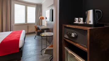 Quarto de hotel com cama, escrivaninha, cadeira, cafeteira e televisão.