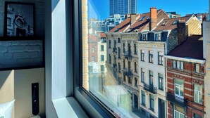 Quarto com uma grande janela que oferece vista para a paisagem urbana, com edifícios históricos e um arranha-céu moderno.