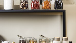 Uma bancada de cozinha com diversos potes de ingredientes e temperos, uma cafeteira branca e um vaso de planta.