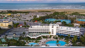 Um hotel com várias piscinas, uma praia e vista para o oceano.