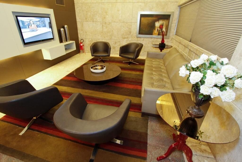 Uma sala de estar moderna com um sofá, duas poltronas, uma mesa de centro e uma TV fixada na parede.