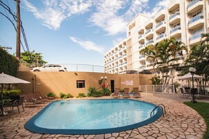 Um hotel com piscina, espreguiçadeiras e um edifício de vários andares com varandas.
