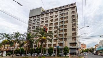 Um hotel de vários andares com fachada uniforme, aparelhos de ar condicionado e uma faixa de pedestres.