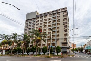 Um hotel de vários andares com fachada uniforme, aparelhos de ar condicionado e uma faixa de pedestres.
