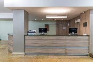 Uma área de recepção com balcão de madeira, dois monitores, uma TV de tela plana e um aparelho de ar condicionado fixado na parede.