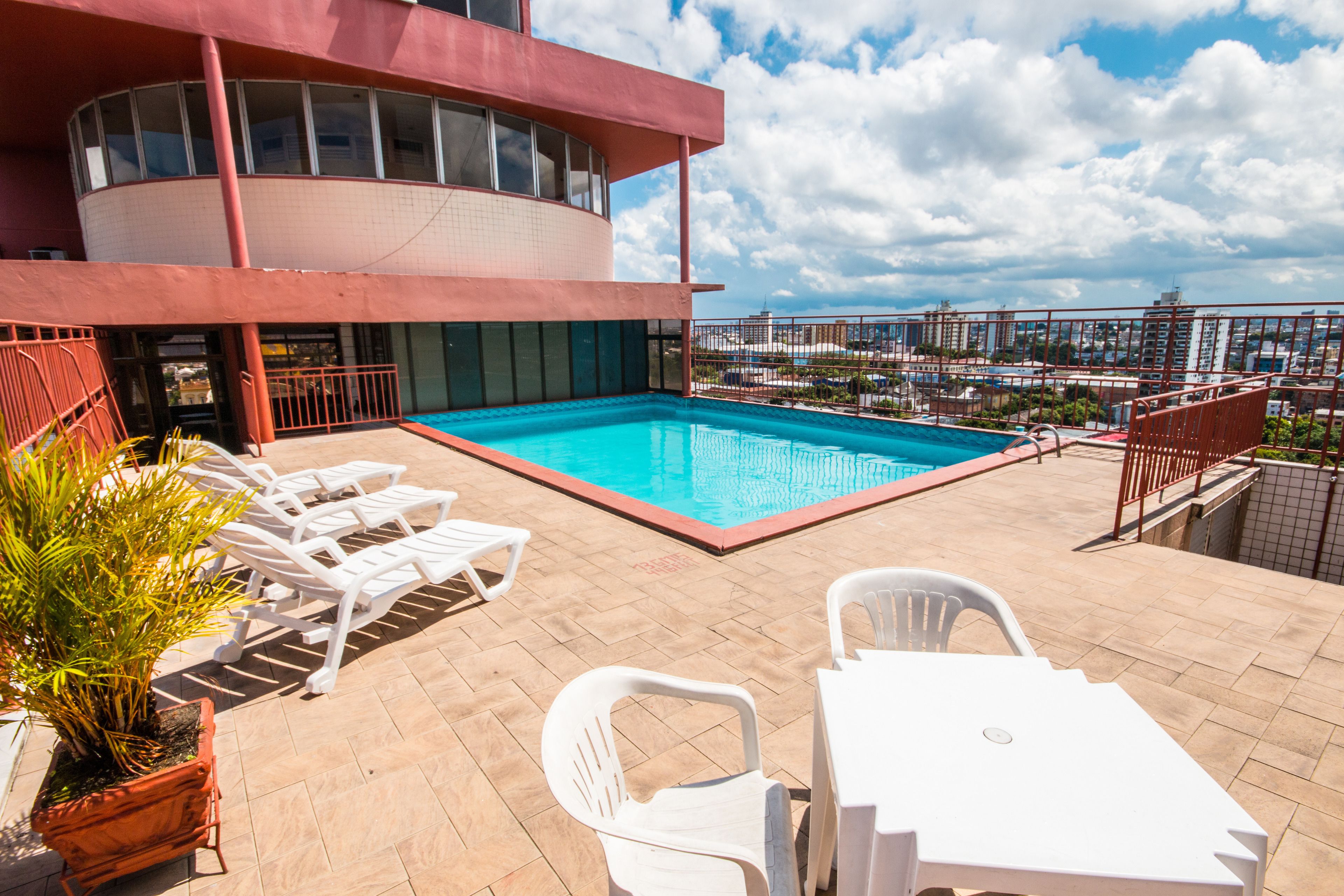 Área de piscina no terraço com cadeiras de lounge brancas, uma mesa e um vaso com planta.