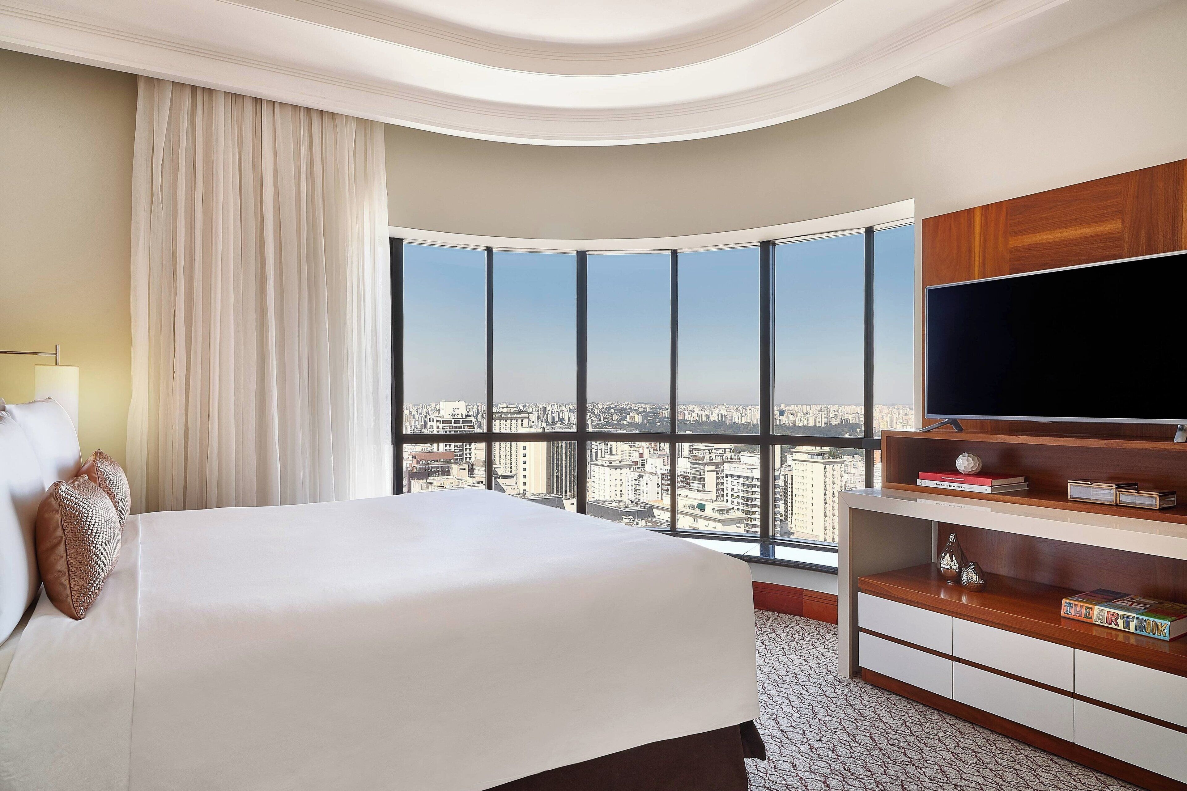 Quarto de hotel com cama grande, televisão e vista para a cidade.