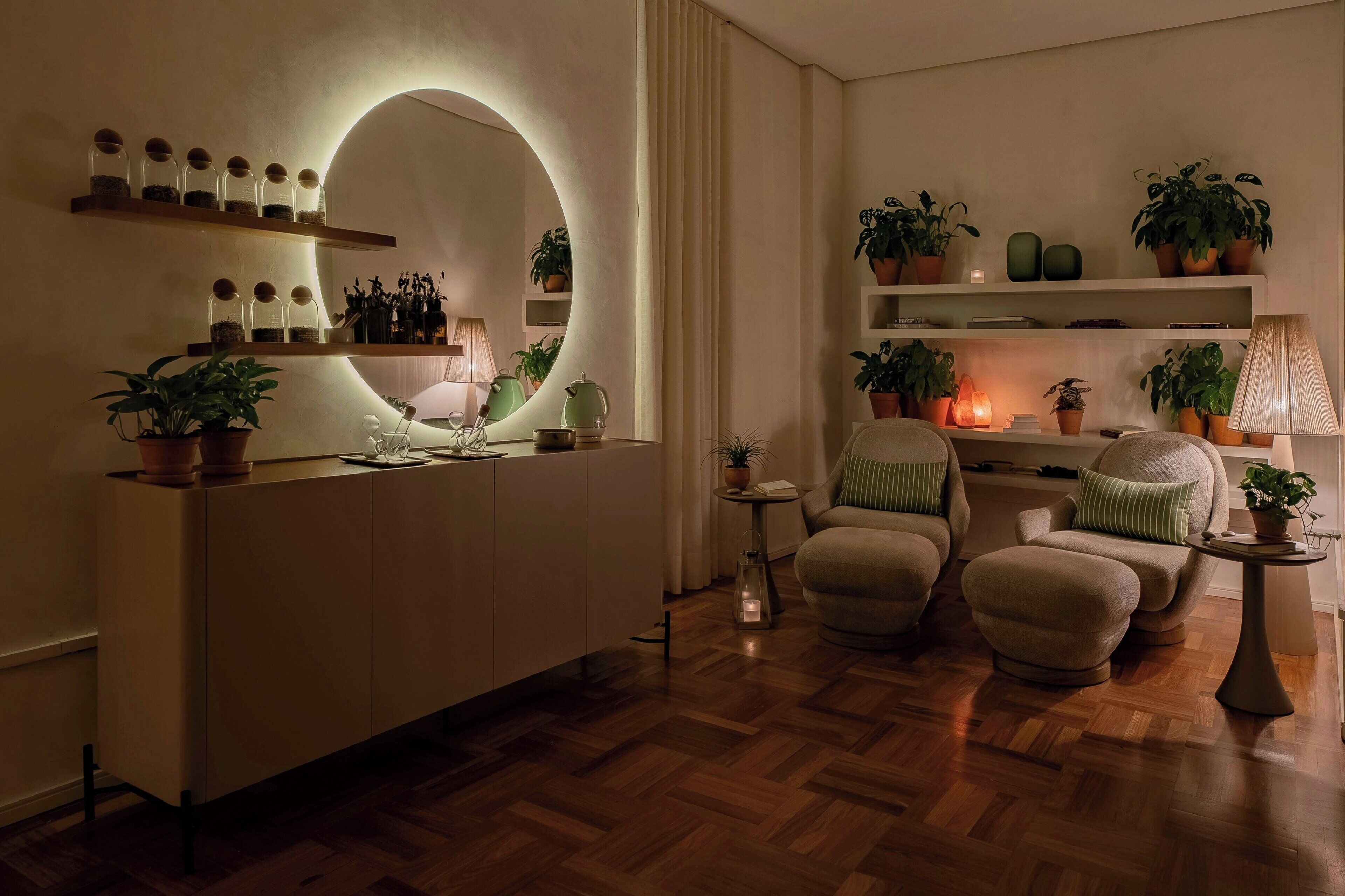 Uma sala de estar moderna com piso de madeira, um espelho redondo, um sofá e várias plantas em vasos.