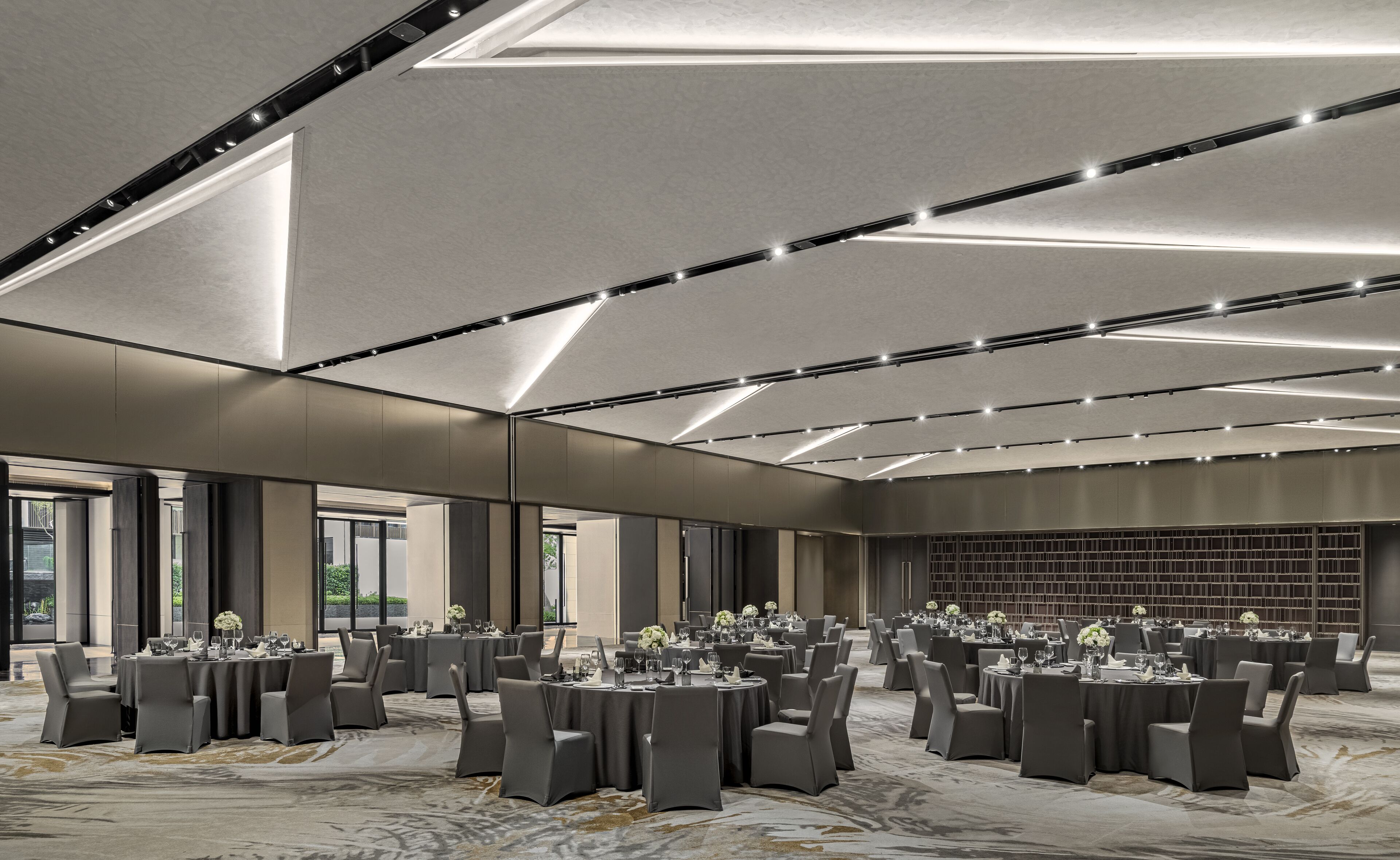 Uma ampla sala de banquetes com várias mesas redondas, cada uma disposta com cadeiras e louças.
