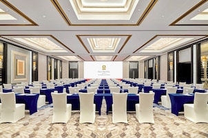 Uma sala de conferências com fileiras de mesas e cadeiras, uma tela grande exibindo o logotipo e um tapete estampado.