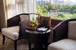 Uma varanda com duas cadeiras de vime, uma mesa pequena com uma cesta de frutas, um guardanapo dobrado e uma placa de madeira decorativa.