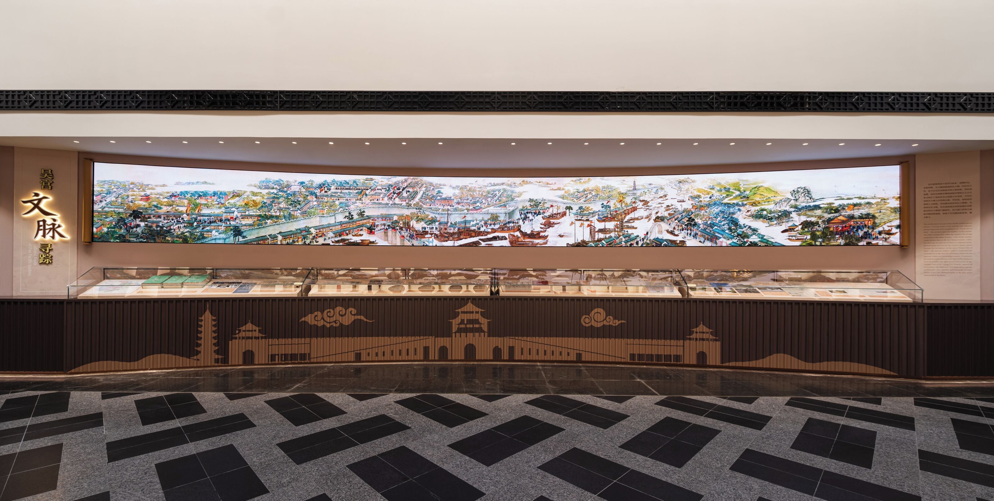 Um hall amplo com um grande painel digital exibindo uma vista urbana, um balcão de recepção com displays informativos e um piso com padrão.