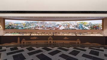 Um hall amplo com um grande painel digital exibindo uma vista urbana, um balcão de recepção com displays informativos e um piso com padrão.