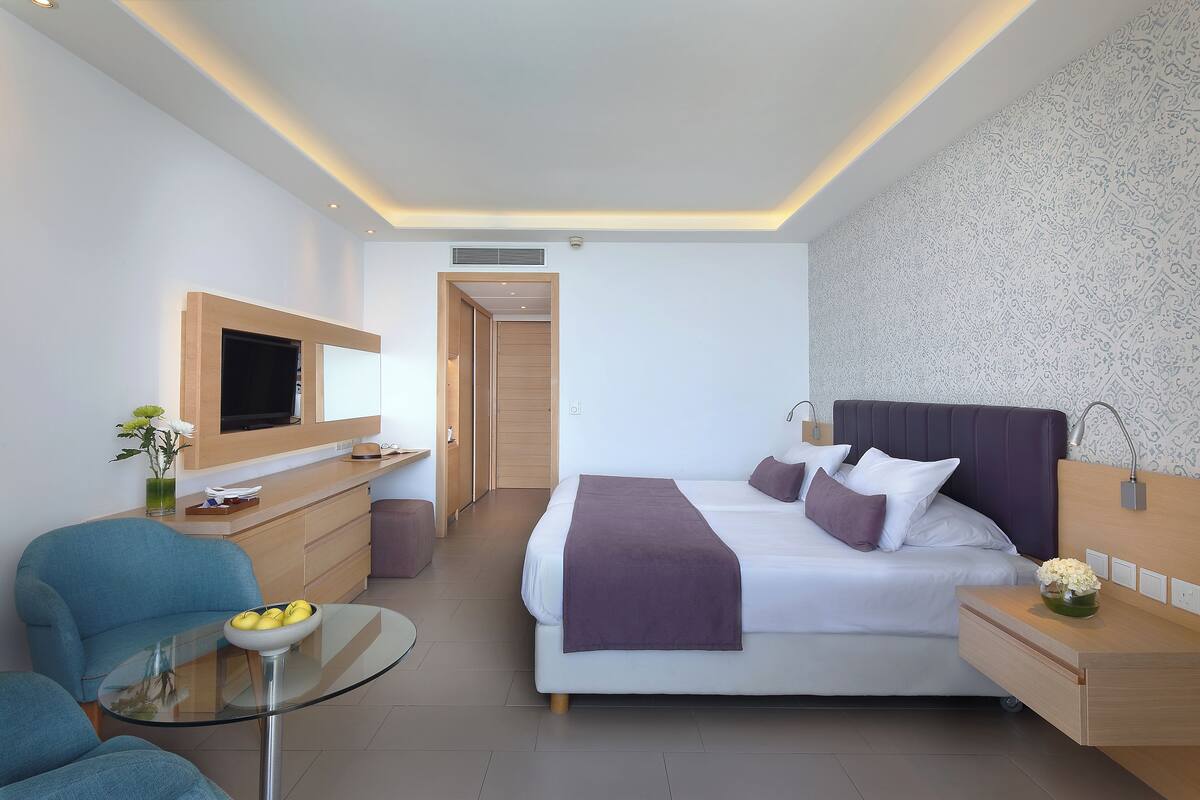 Quarto de hotel moderno com cama, televisão, escrivaninha e área de estar.
