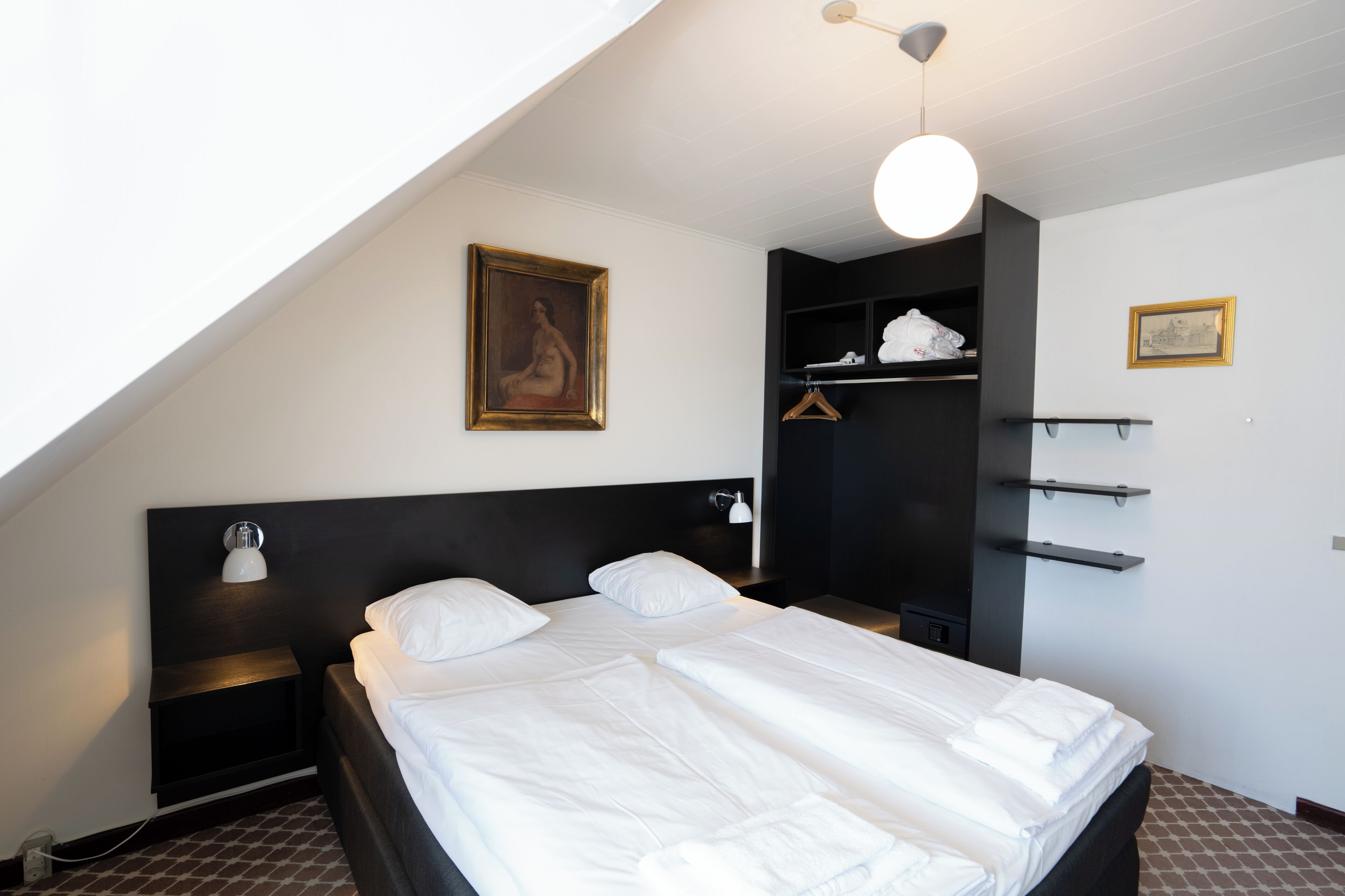Quarto de hotel moderno com uma cama grande, mesa de cabeceira, prateleira na parede e luminária no teto.