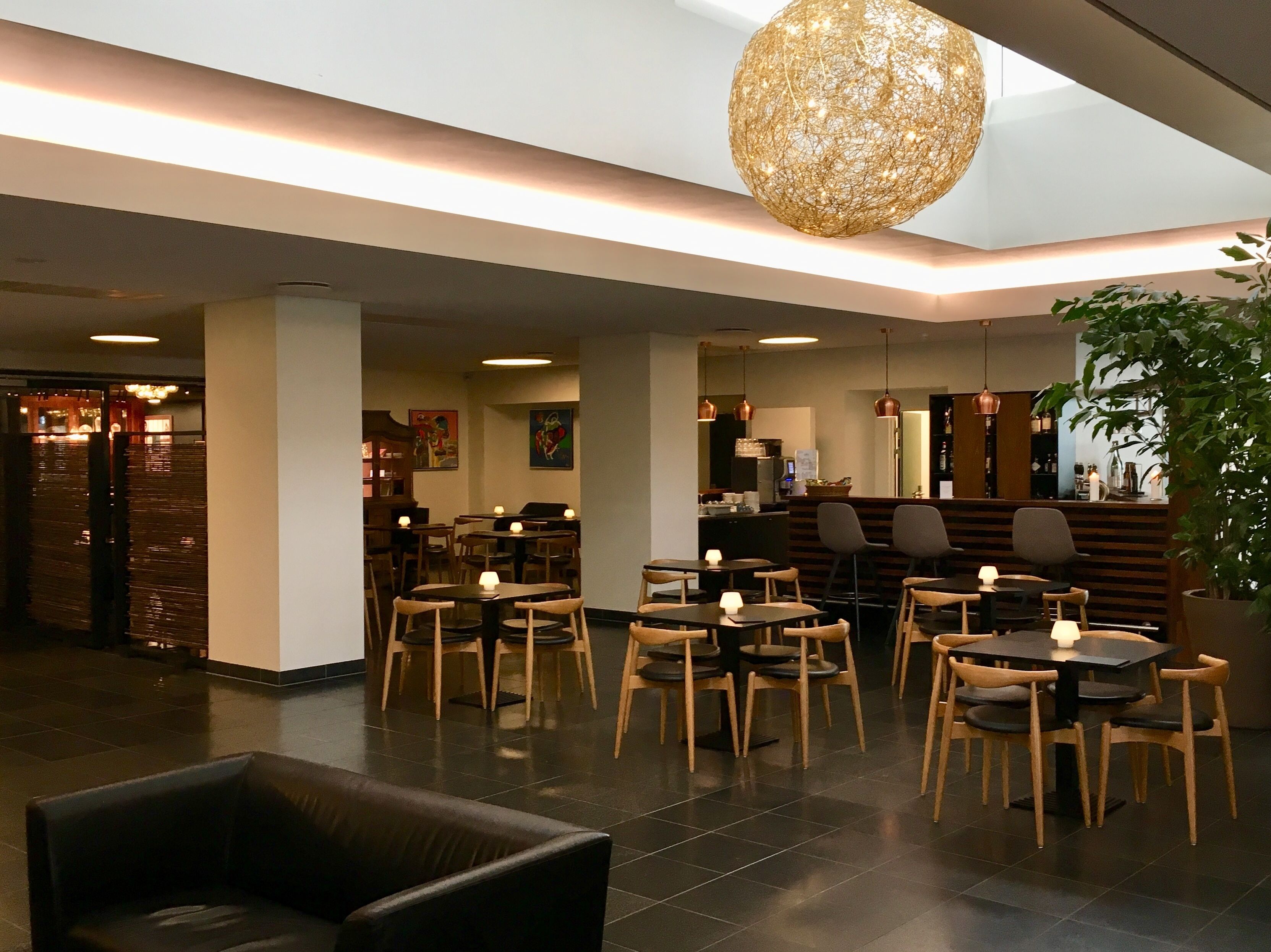 Um hall de hotel moderno com várias áreas de estar, uma mesa de recepção e um grande lustre decorativo.