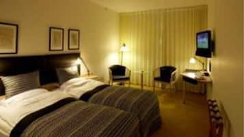 Quarto de hotel com duas camas, uma mesa de trabalho com computador, uma cadeira e televisão.
