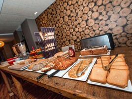 Mesa de buffet com diversos pães e doces, uma torradeira e uma garrafa de suco de maçã.