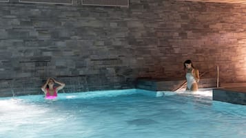 Piscina interior com paredes de pedra e teto de madeira.
