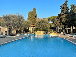 Uma área de piscina com espreguiçadeiras, um pequeno gazebo e um muro de pedra com escadas que levam a um edifício.