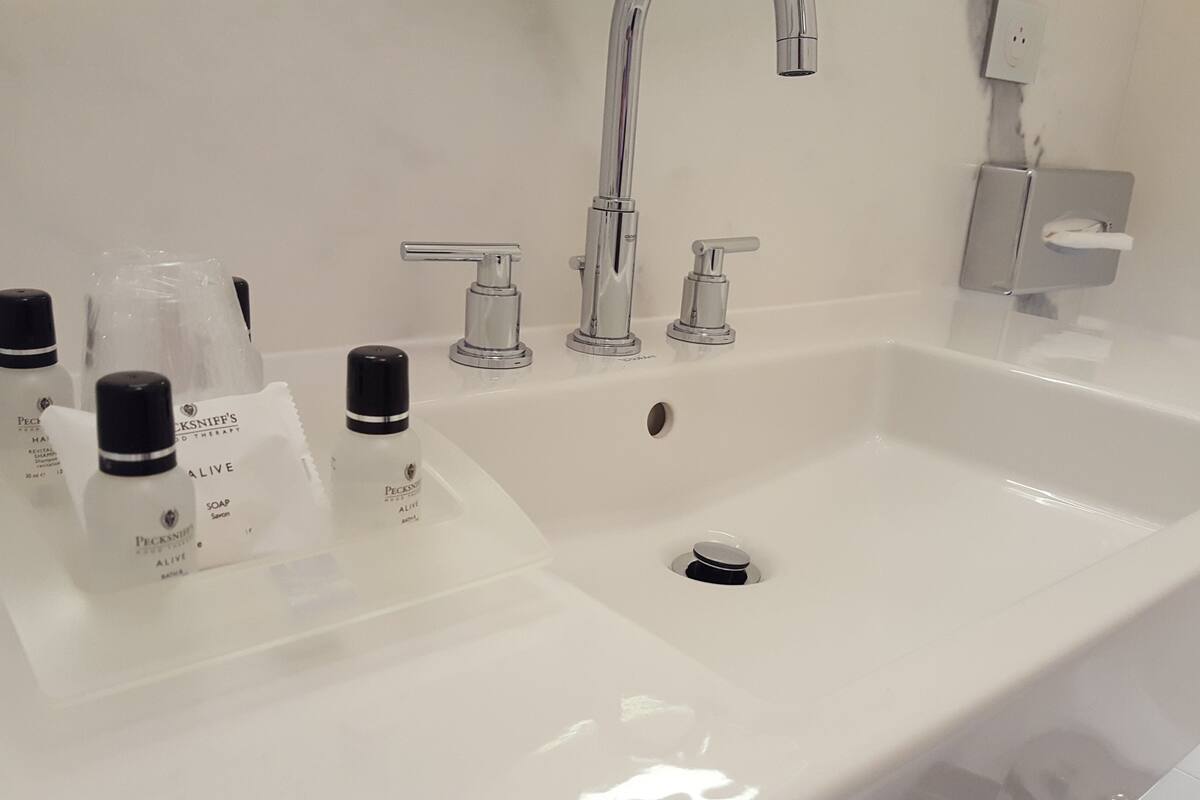 Casa de banho moderna com uma grande pia branca, duas torneiras e vários artigos de higiene pessoal.