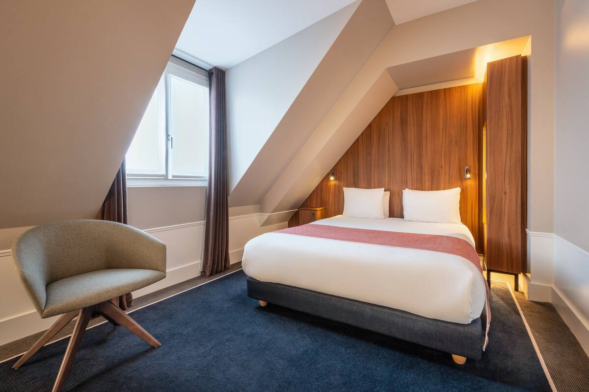 Quarto de hotel moderno com uma cama, uma cadeira e uma janela.