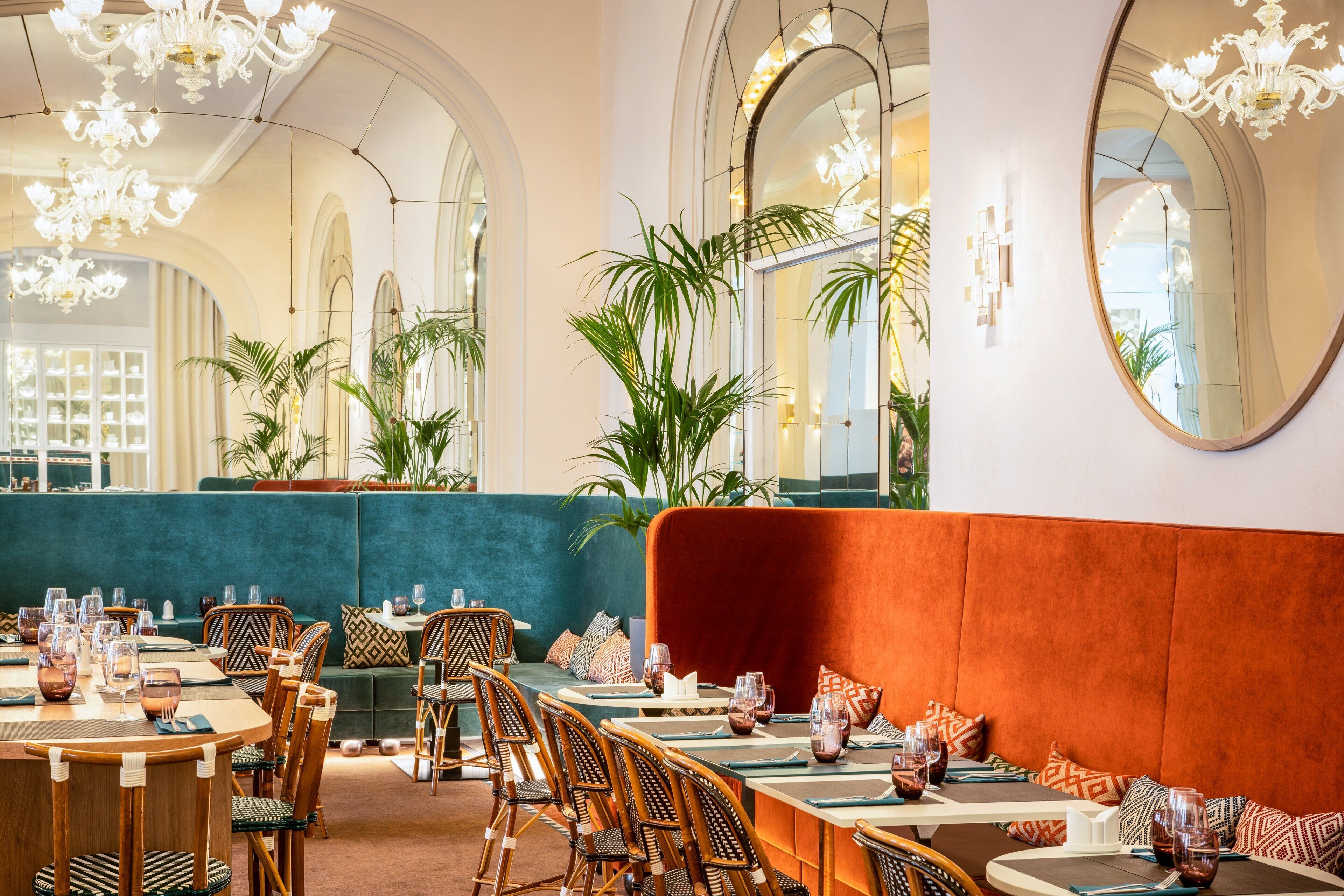 Um restaurante com mesas redondas, assentos acolchoados e lustres pendurados.