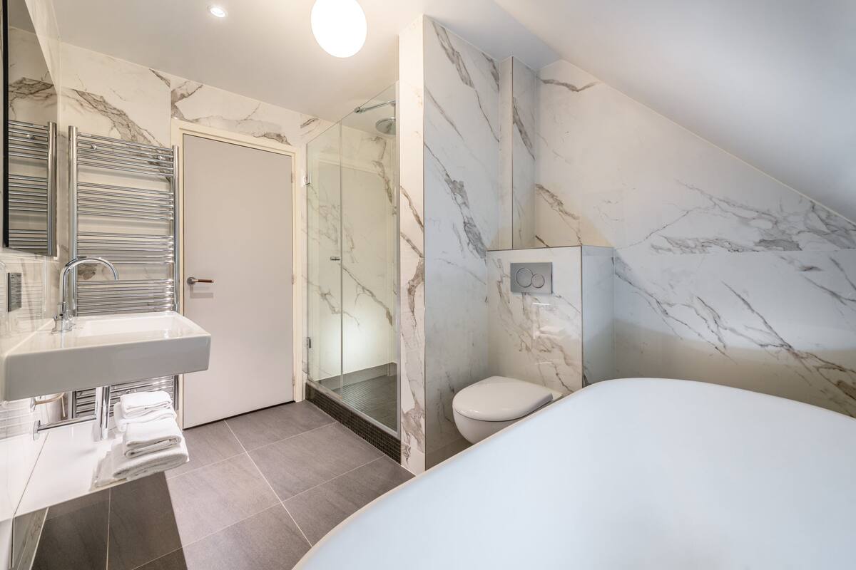 Um banheiro moderno com parede de mármore, box de vidro, pia branca e vaso sanitário.
