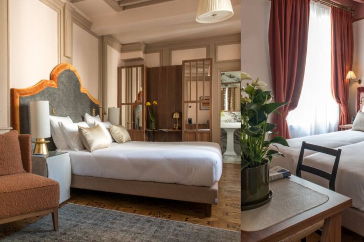 Quarto de hotel com duas camas, área de estar com uma poltrona, mesa e uma janela grande com cortinas.