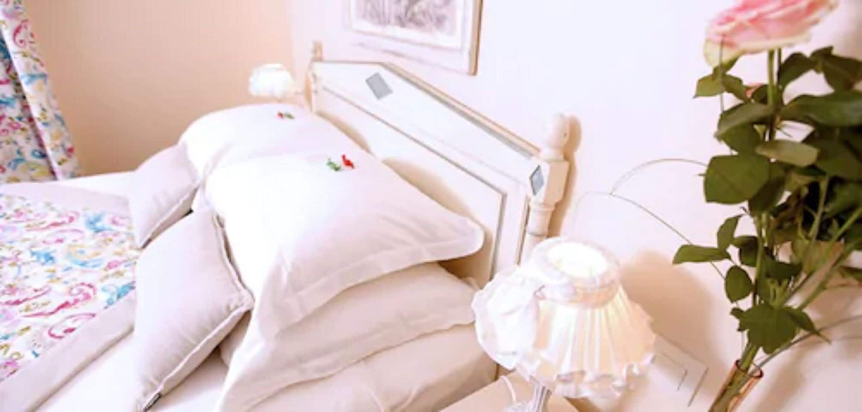 Cama com roupa de cama branca e uma única rosa em um vaso.