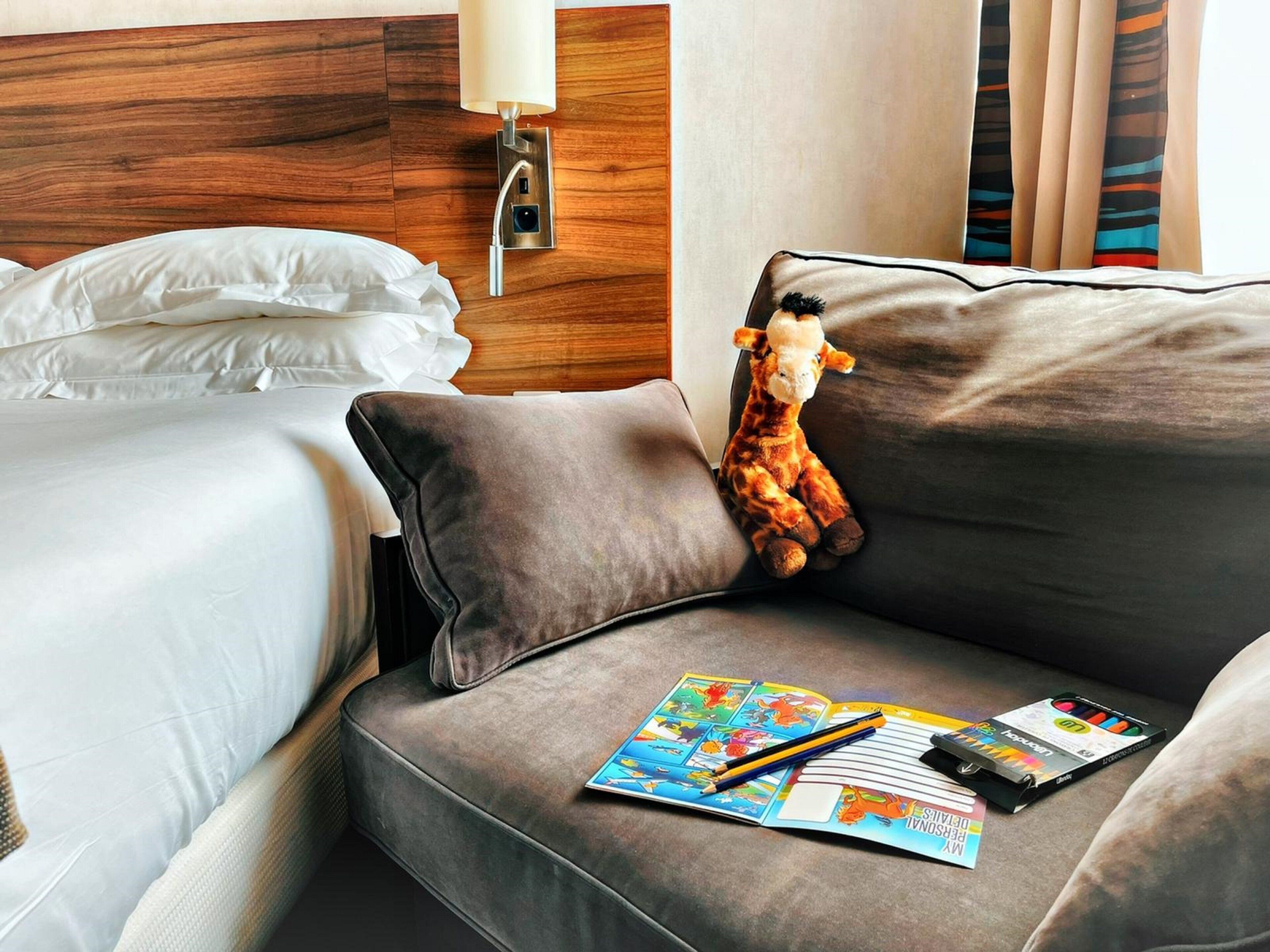 Quarto de hotel com uma cama, um sofá, um abajur e um brinquedo de girafa de pelúcia.