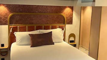 Quarto de hotel moderno com uma cama grande, uma televisão de tela plana acima da cama e uma mesinha de cabeceira.