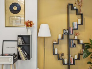 Quarto com estante de livros, toca-discos, abajur e prateleira na parede com livros e velas.