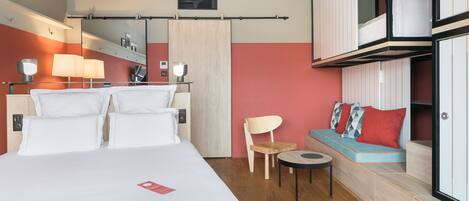 Quarto de hotel com uma cama grande, uma mesa pequena, uma cadeira, um sofá, um espelho e um guarda-roupa.