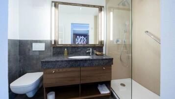 Um banheiro moderno com pia de mármore, penteadeira de madeira, box de vidro e vaso sanitário.