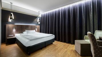 Quarto de hotel moderno com uma cama grande, mesas de cabeceira, uma escrivaninha e uma cadeira.