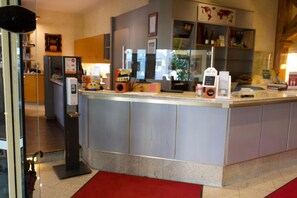 Uma área de recepção de hotel com balcão, máquina de café, sinal de Wi-Fi e um pequeno frigorífico.