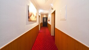 Um corredor de hotel com carpete vermelho, painéis de madeira e um candelabro.