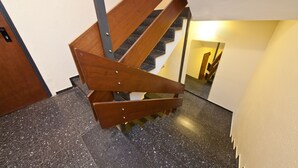Uma escada de madeira com corrimão de metal, que leva a um patamar com uma porta.