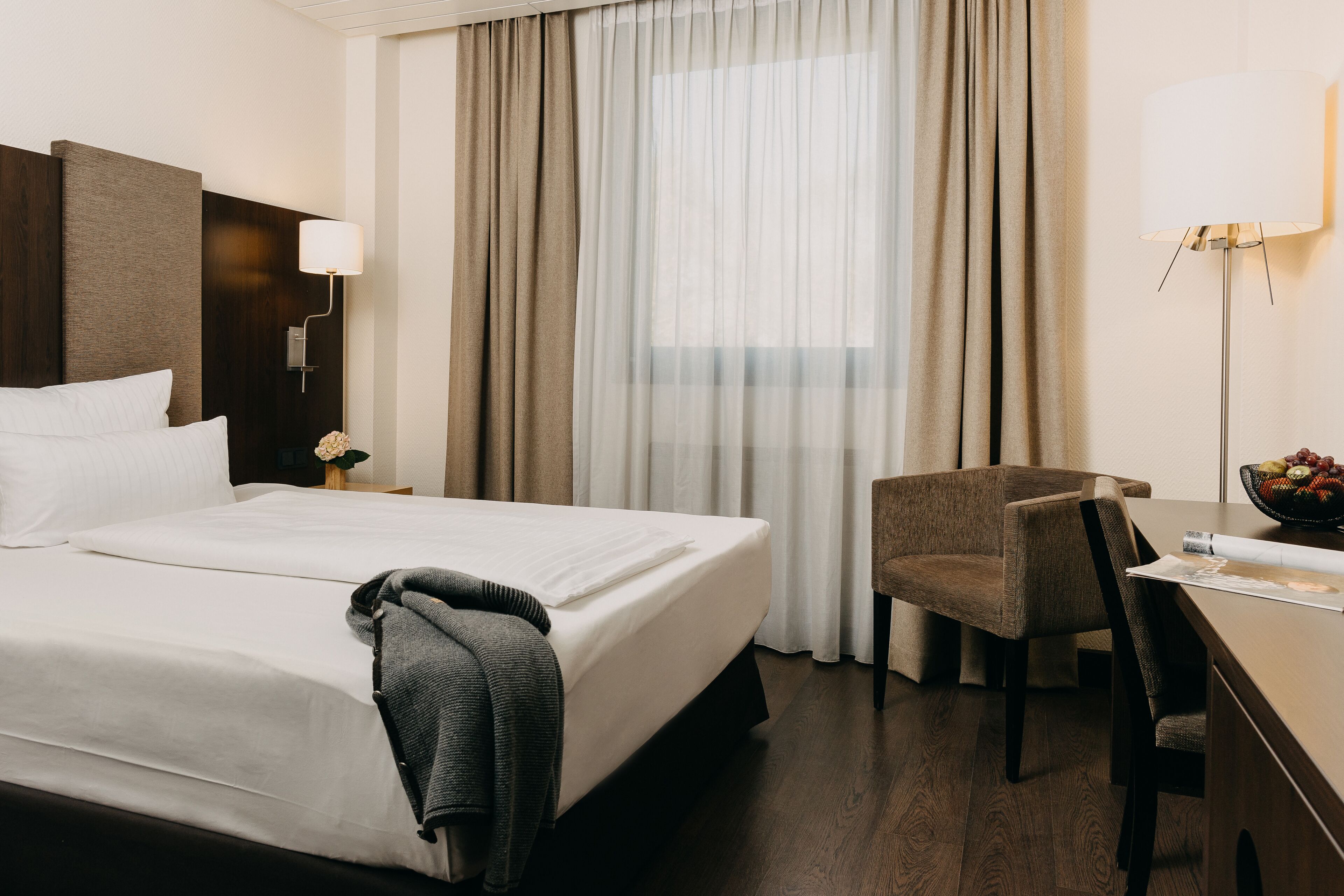Quarto de hotel com uma cama grande, uma escrivaninha com abajur e uma cadeira.