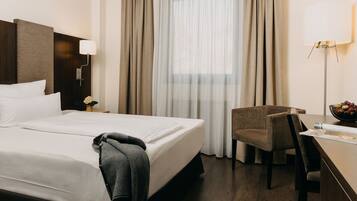 Quarto de hotel com uma cama grande, uma escrivaninha com abajur e uma cadeira.