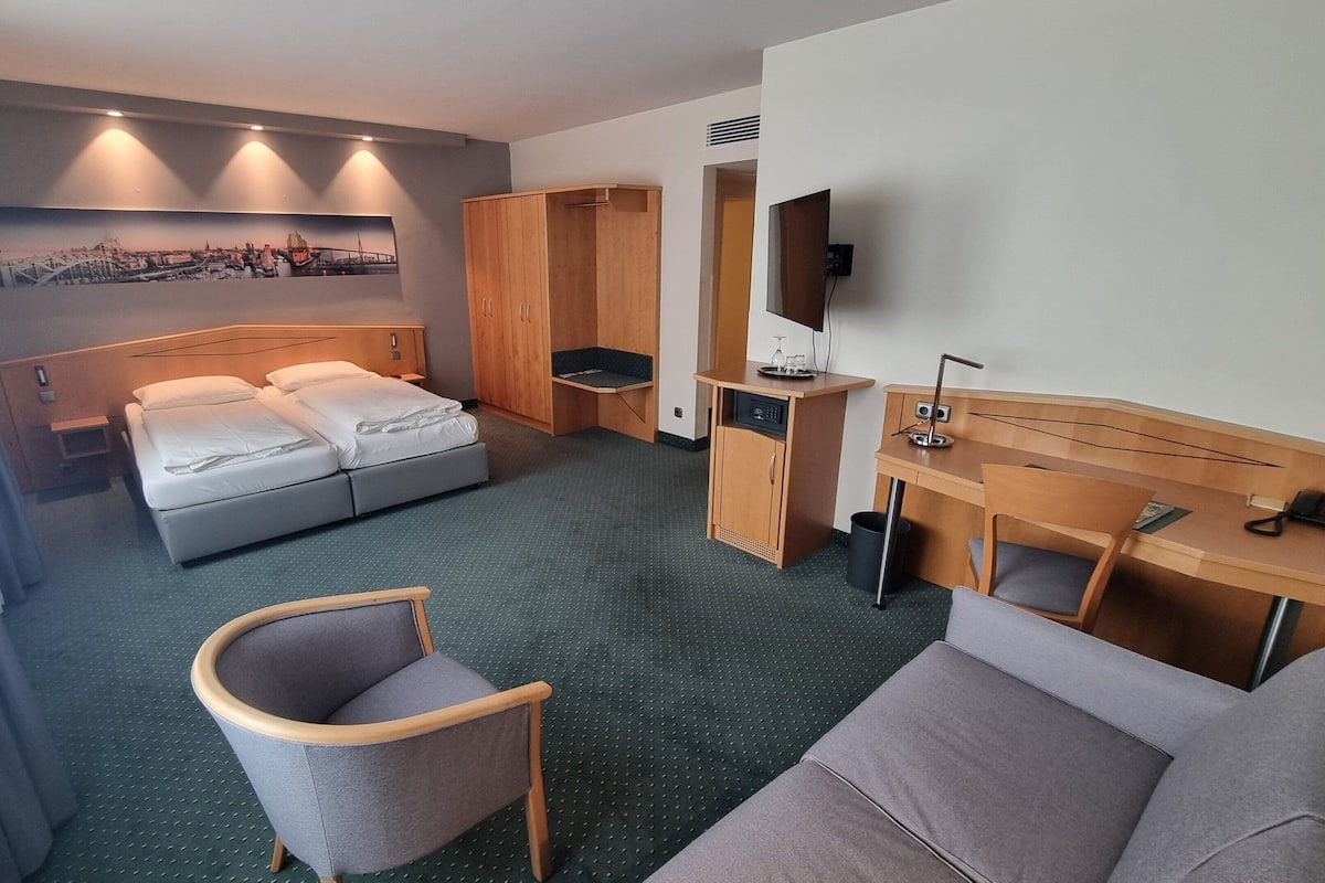 Quarto de hotel com uma cama, uma escrivaninha, uma cadeira, uma televisão e um quadro na parede.